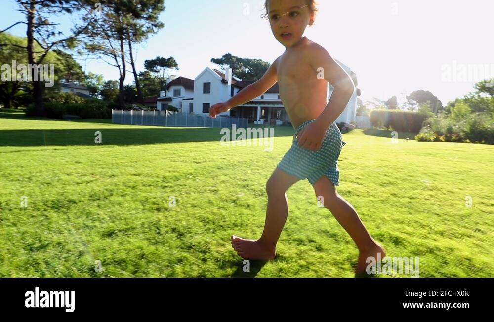 Toddler baby boy running outside in home garden with sunlight lens ...