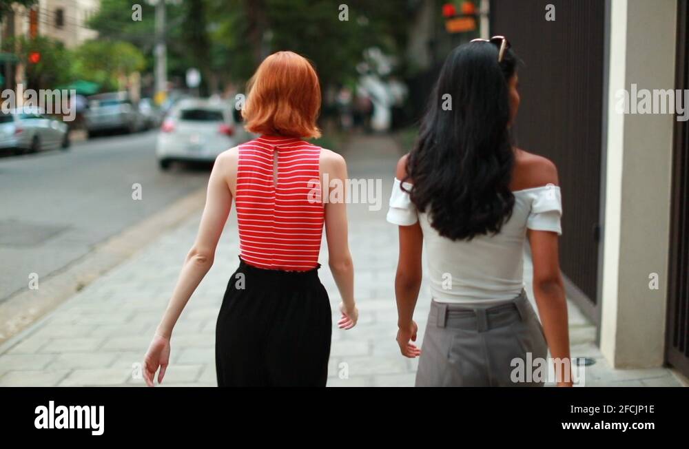 Back view of two young women walking together in city. Pretty ...