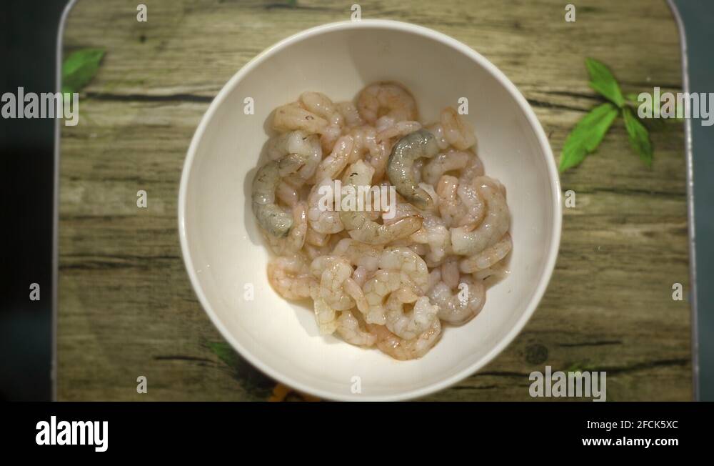 Peeling a prawn and dropping it into a bowl of cleaned prawns from sea ...
