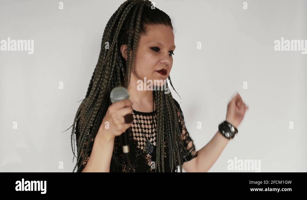 A gothic girl with long grey afro braids is singing to a microphone ...