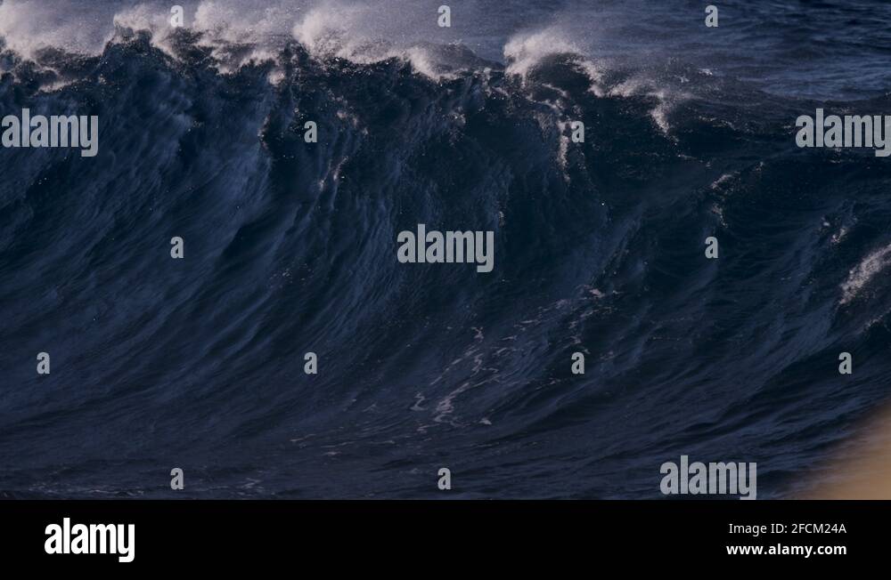 A wave forms into a wall ofing water along a shallow rock shelf. Slow ...