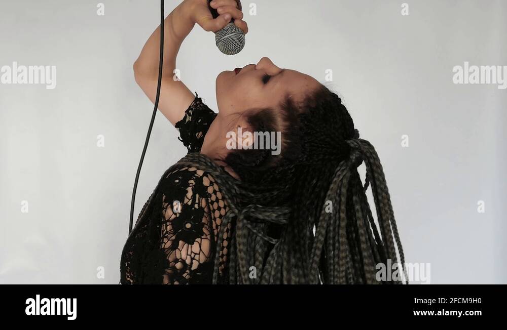 A gothic girl with long grey afro braids is singing to a microphone ...