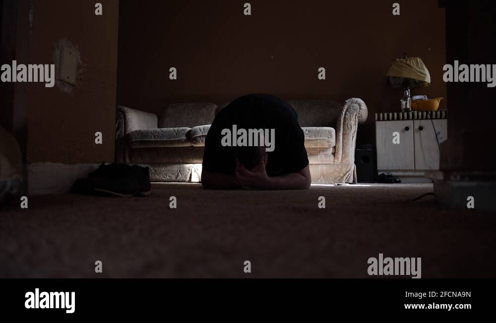 A depressed, sad man lays on floor in apartment crying and praying ...