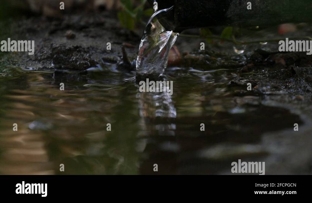 Tilt up from a puddle to reveal a pipe with a stream of water flowing ...