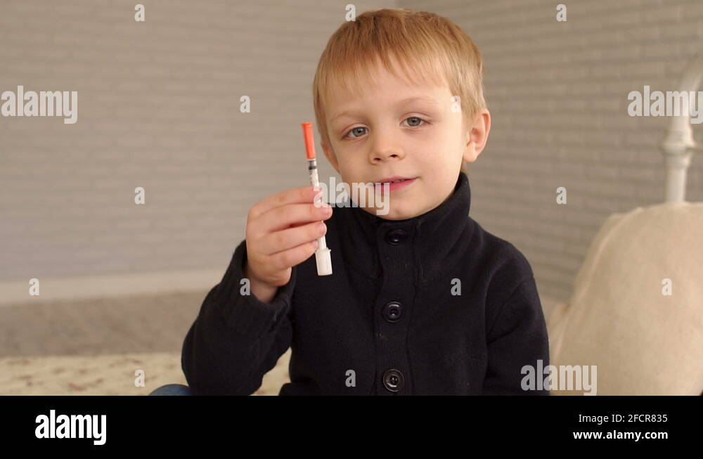 A little boy sitting on the bed at home and holding an insulin syringe ...