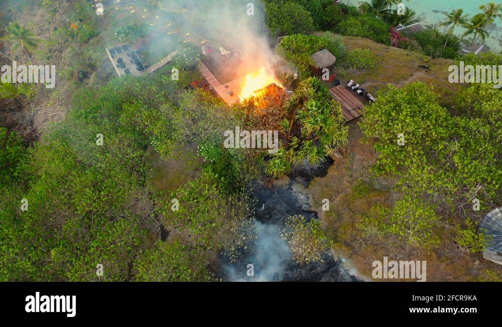 Aerial of a straw hut burning on a beautiful tropical island, Fireman ...