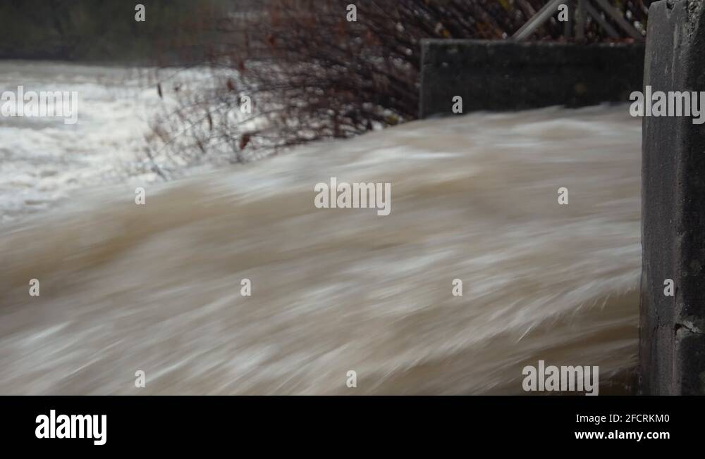 Static view of dirty river violently flooding over small canal into ...