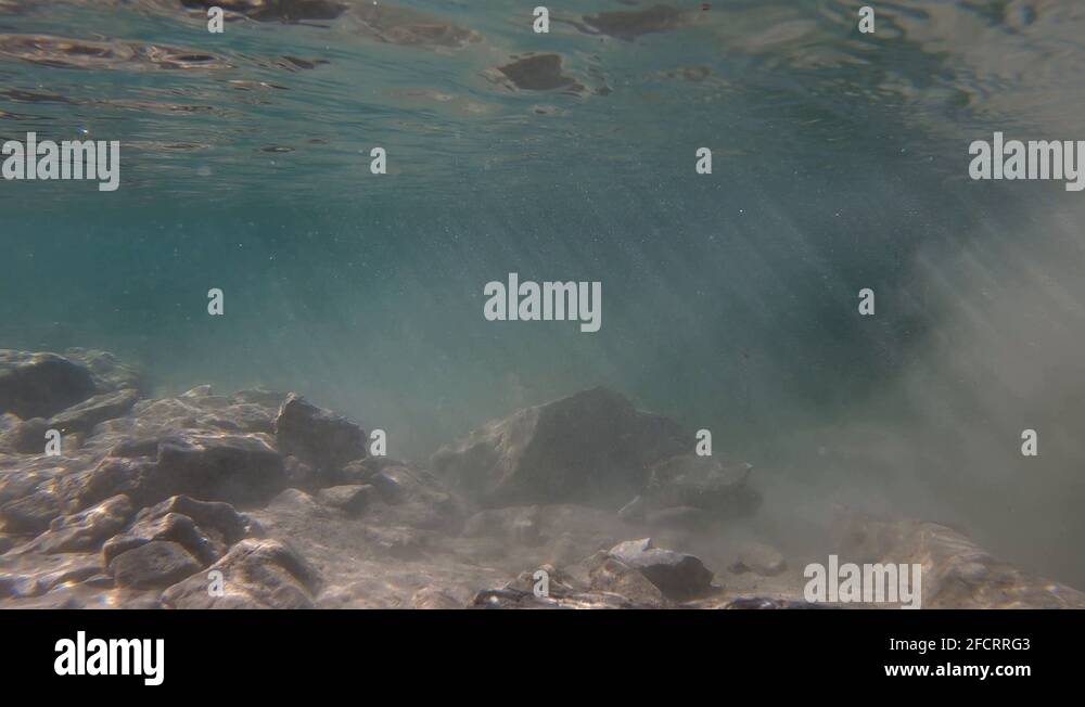 Slow motion underwater sun rays hitting lake water rock falling on ...