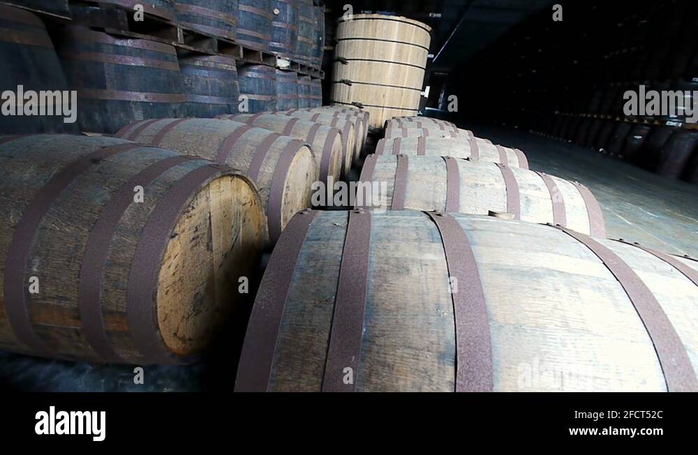 Rows of whiskey barrels laying on their side in a warehouse filled with ...