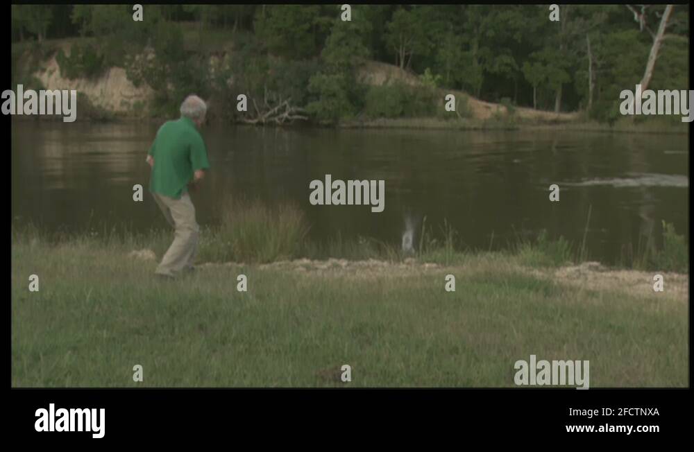 2000s: UNITED STATES: man skims water with stones. Girl and boy talk to ...