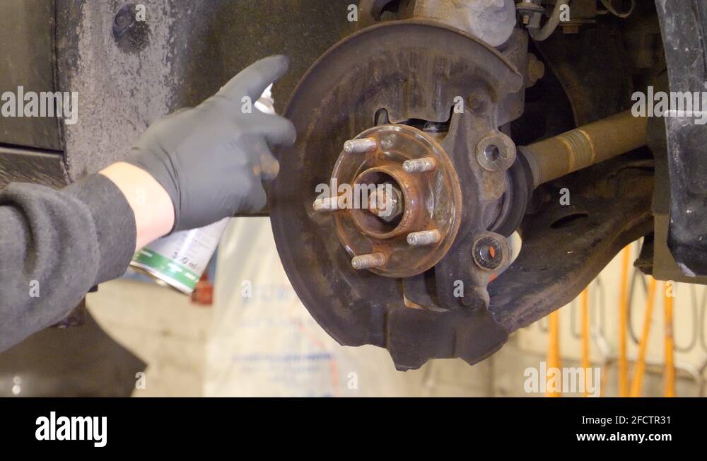 Mechanic spraying lubricant on a rusty wheel stud before replacing the ...