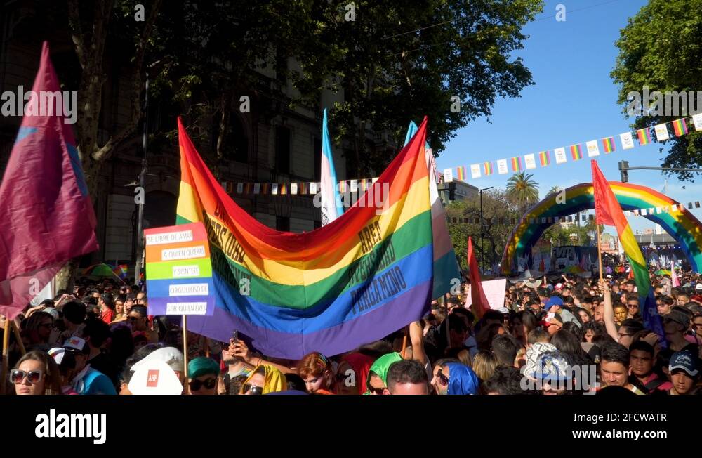 Crowd of people carrying rainbow flags down the street at Pride Parade ...