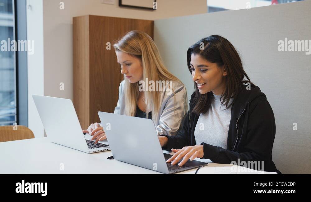 Two Young Businesswomen With Laptops Working Side By Side In Modern ...