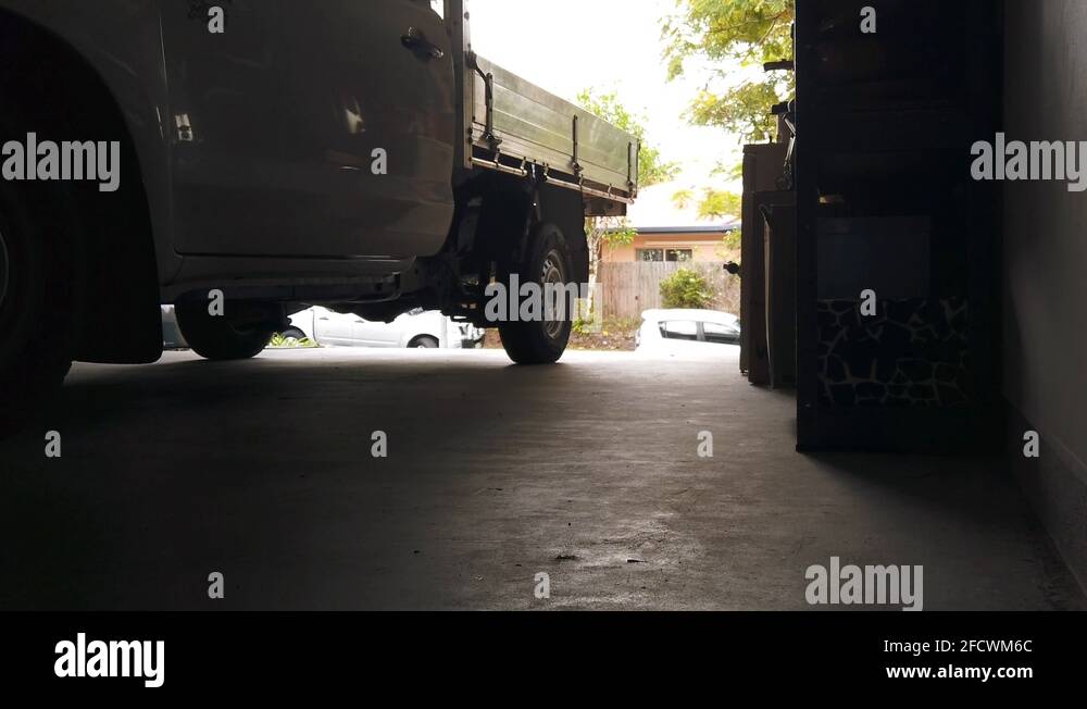 silhouette of a man in long pants exiting a ute suv in a garage carport ...