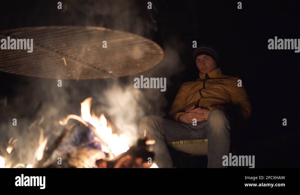 Adult Male Sitting Beside Campfire and Grill. Low Angle And Locked Off ...