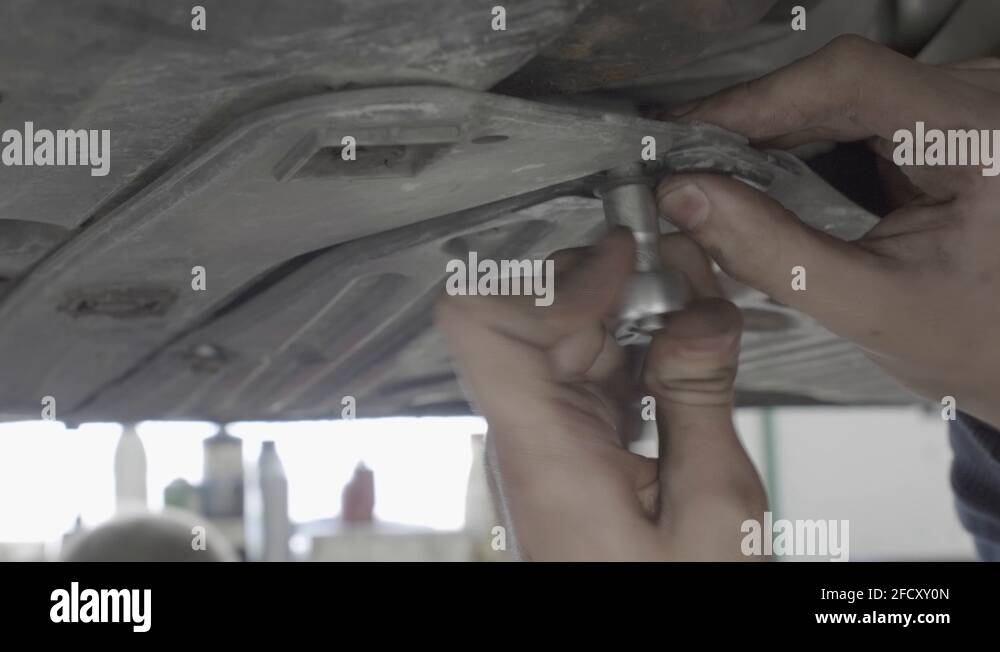 Mechanic applying torque with a wrench to screw a bolt on a car in an ...