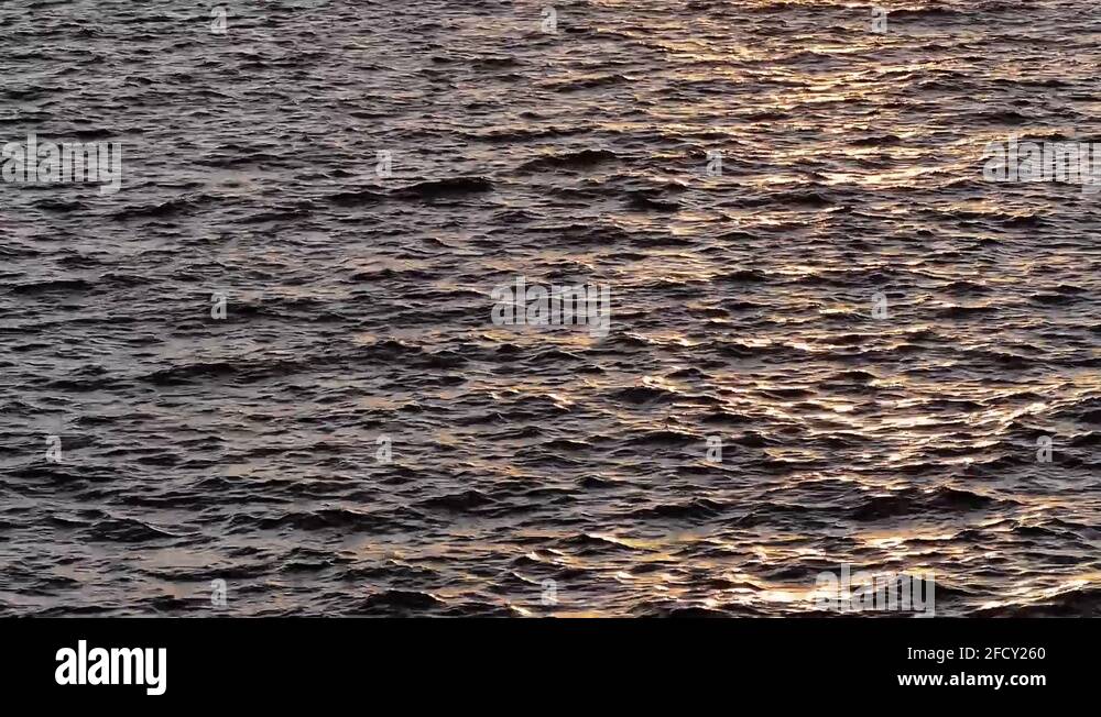 Small waves on the ocean ripple with low sunlight. Static handheld long ...