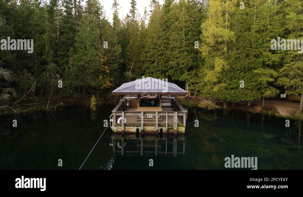 Wooden tourist raft on lake, aerial pedestal up to reveal lush forest ...