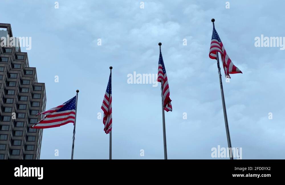 American flags flying against a cloudy sky with a skyscraper in view ...