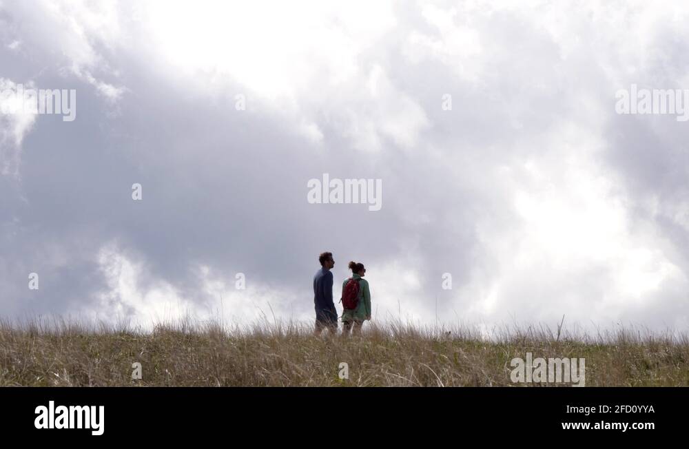 Romantic couple embrace on windy, overcast, stormy hillside top ...
