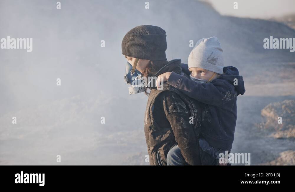 A survivor mother carring her son in gas mask going through clouds of ...