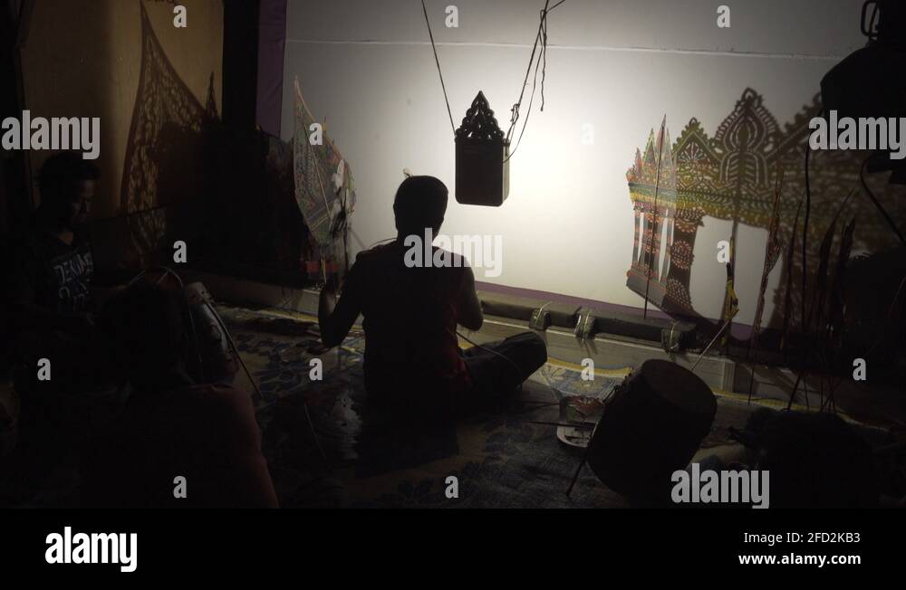 A traditional shadow puppet master playing skillfully behind the white ...