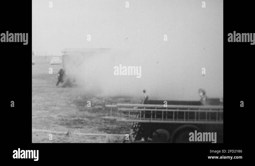 1950s: FIreman pulls fire hose over to smoking building. Man rinses out ...