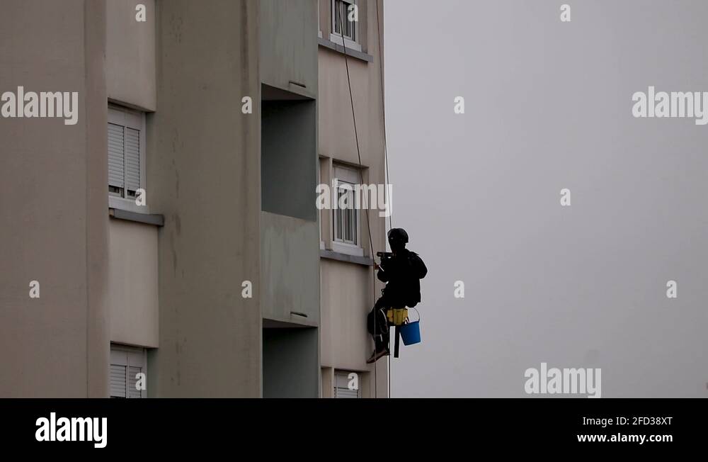 Worker Climber Hanging On Ropes on a High-Rise to maintain the building ...