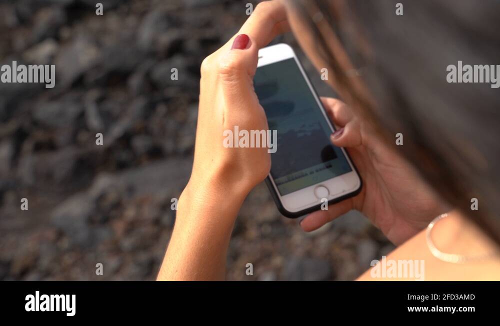 Woman scrolling through beach photos on smartphone, rocky background ...