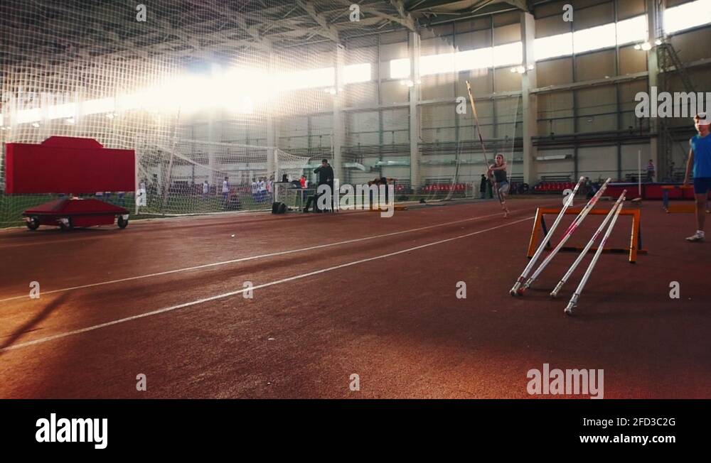 Pole vaulting indoors - a young woman in grey leggins jumping over a ...
