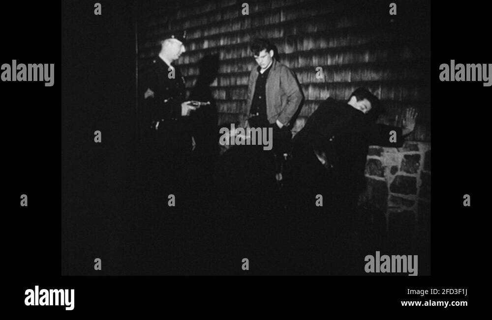 1960s: Detective points gun. Detective frisks boy leaning, hands on ...