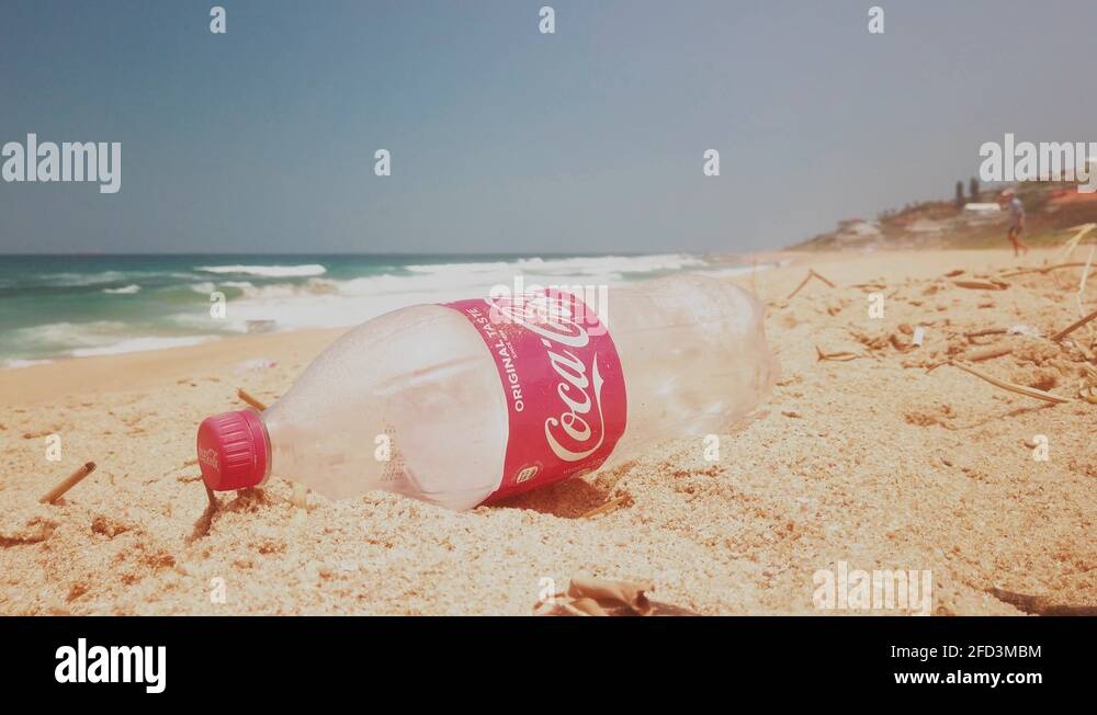 a single coca cola bottle discarded on the beach, crashing waves ...