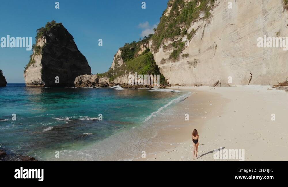 Back view of Woman in bikini walking on beach with sea rocks and ...