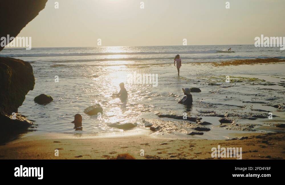 Children with mother bathing in low tide shallow pool at beach in ...
