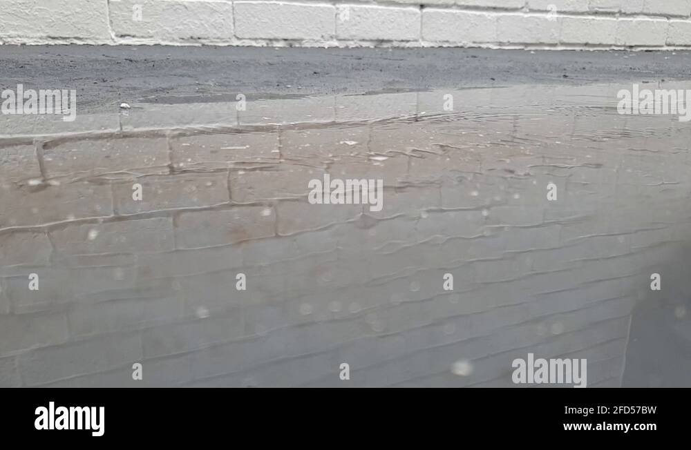 Rain drops falling down and creating ripples on a concrete slab with a ...