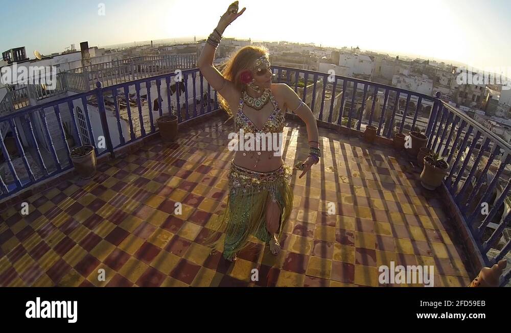 Camera orbits around beautiful belly dancer as she wiggles on the roof ...