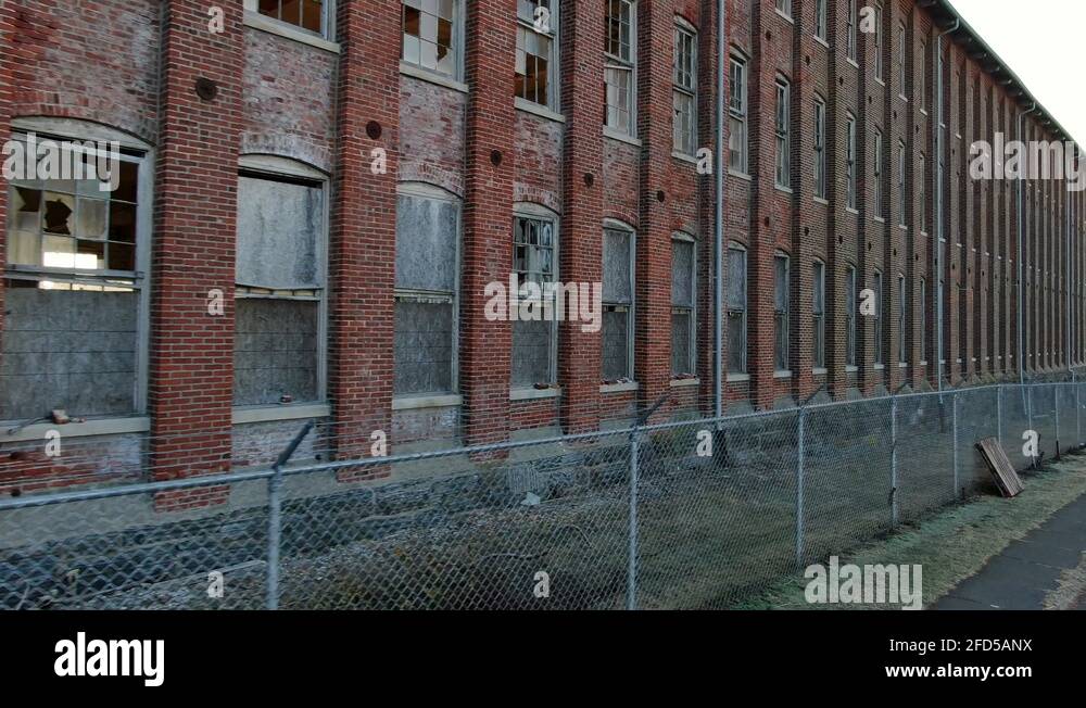 Chain link fence surrounds old boarded-up factory building, now site of ...