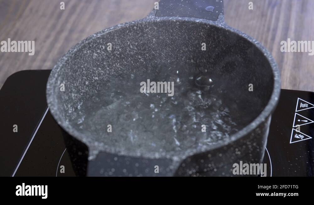 Putting noodles in the hot water inside of a black pot heated by ...