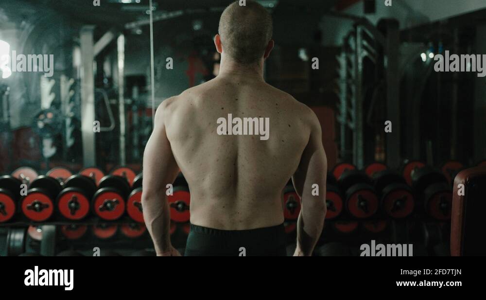 Shirtless muscular bodybuilder standing in front of rows of free ...