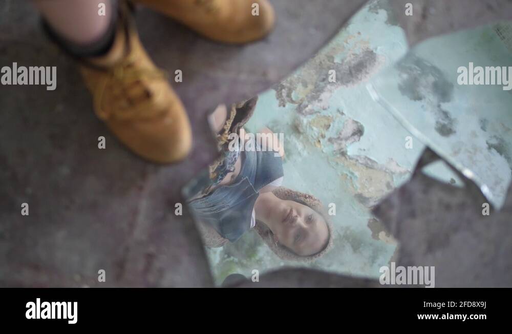 A young woman is smashing pieces of a mirror showing her own reflection ...