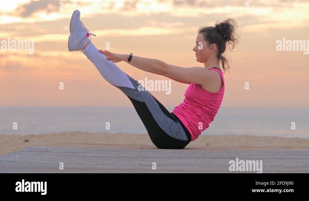 Woman in fitness clothes on the ocean shore doing exercises for the abs ...