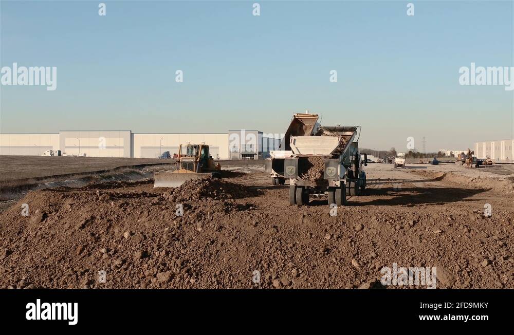 A compact tractor loader pushes and spread soil as a dump truck readies ...