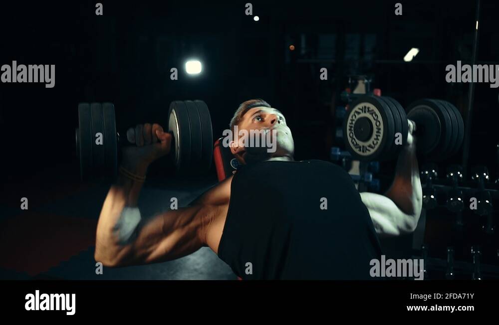 A muscular man performs exercises, raises dumbbells on pectoral muscles ...