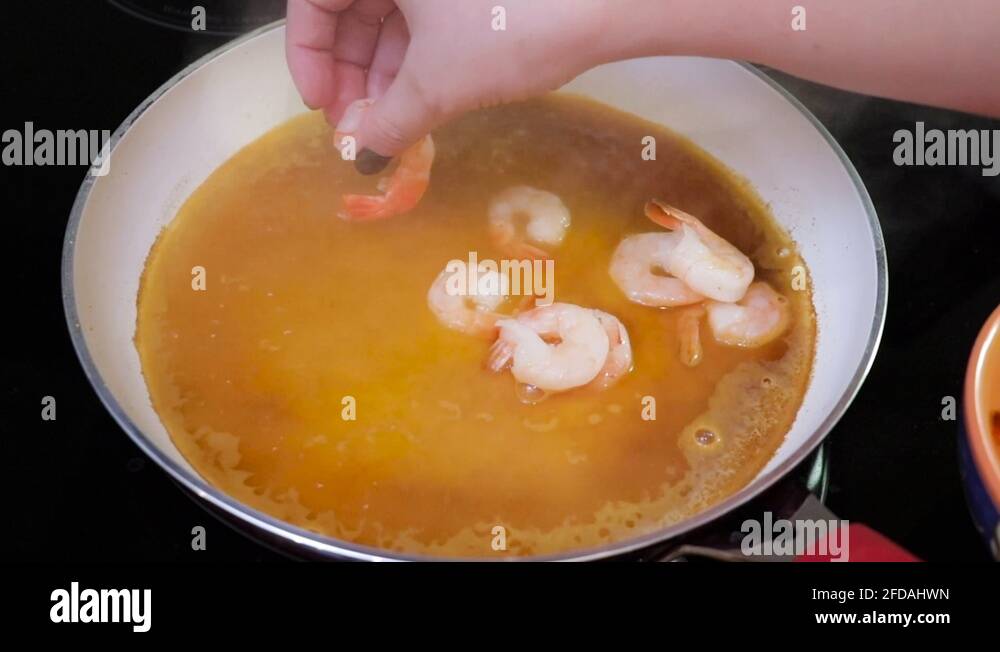 Placing shrimp on frying pan with broth on stovetop to cook them Stock ...
