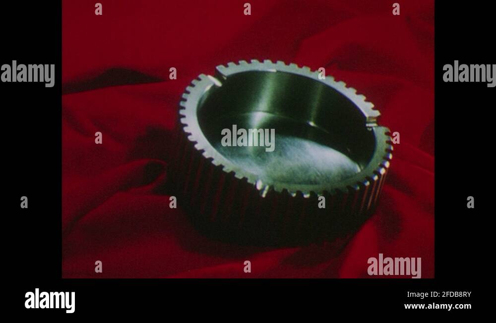 1970s: Round metal gear lies on red cloth. Man looks at designs for ...