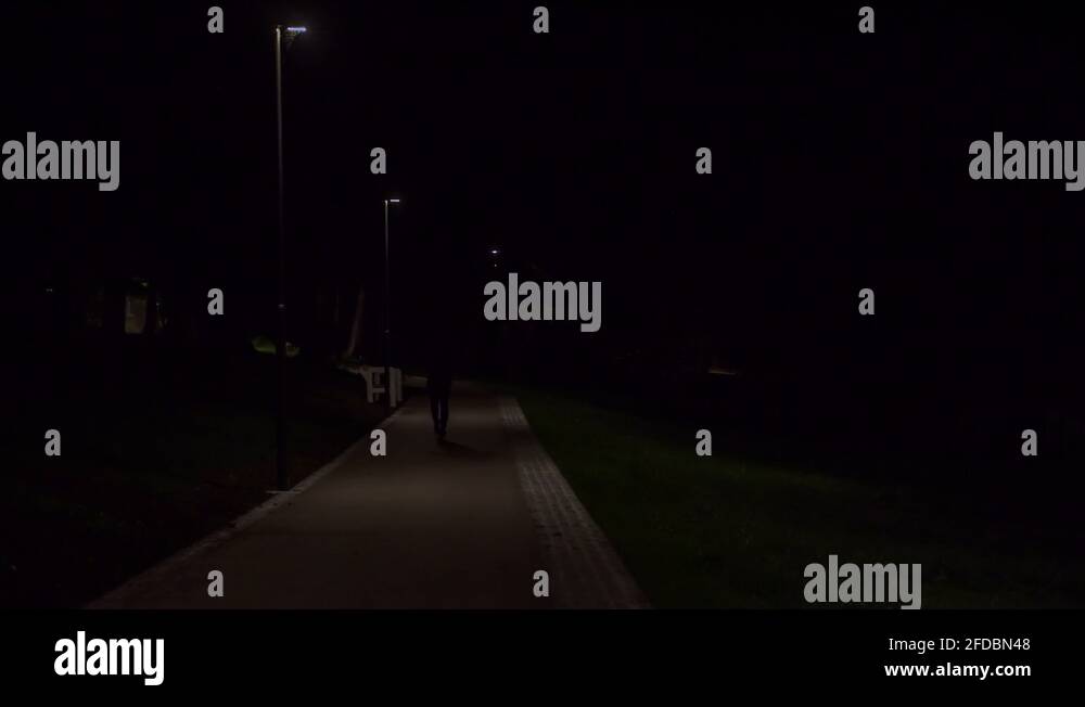 Pan shot, revealing a man running through a park during night time ...