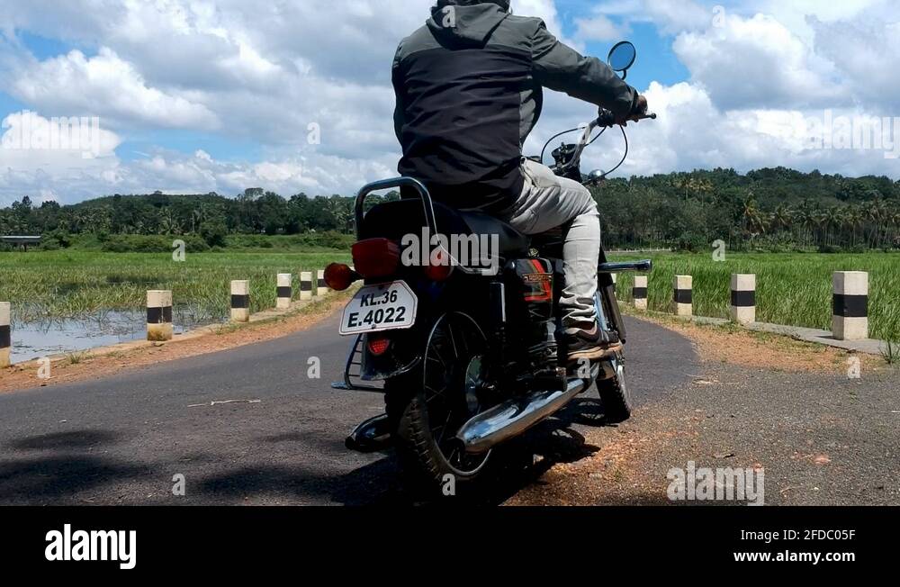 Motorbike rider riding a vintage bike,Indian road,road between water ...