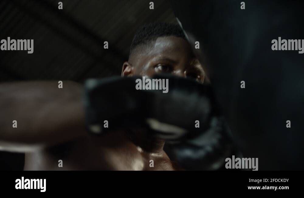 Hand held shot of shirtless man punching and elbowing a heavy bag in ...