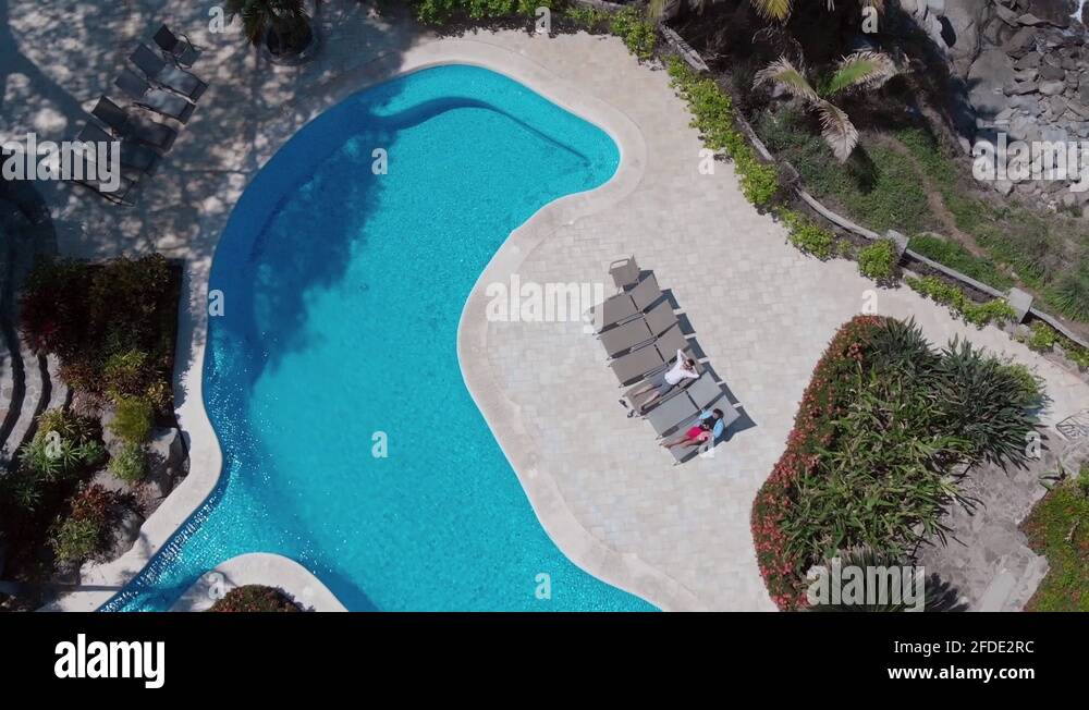 Drone top-down view of two men relaxing around a pool at a luxury ...