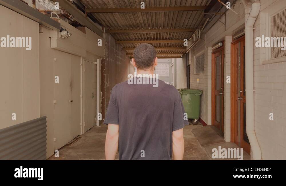 Backview Of A Man Slowly Walking In The Alley With Green Trash bin On ...
